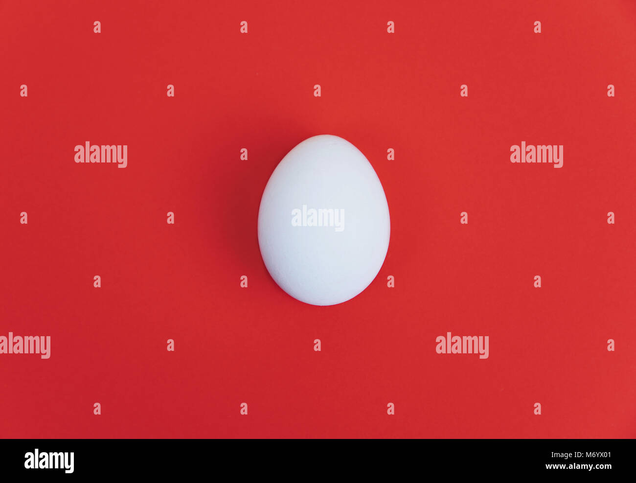One white egg on red background Stock Photo - Alamy