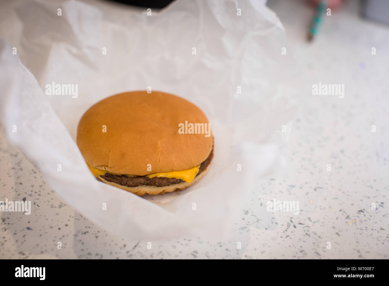 Single cheese burger on a table top in a grease proof paper wrapper ...