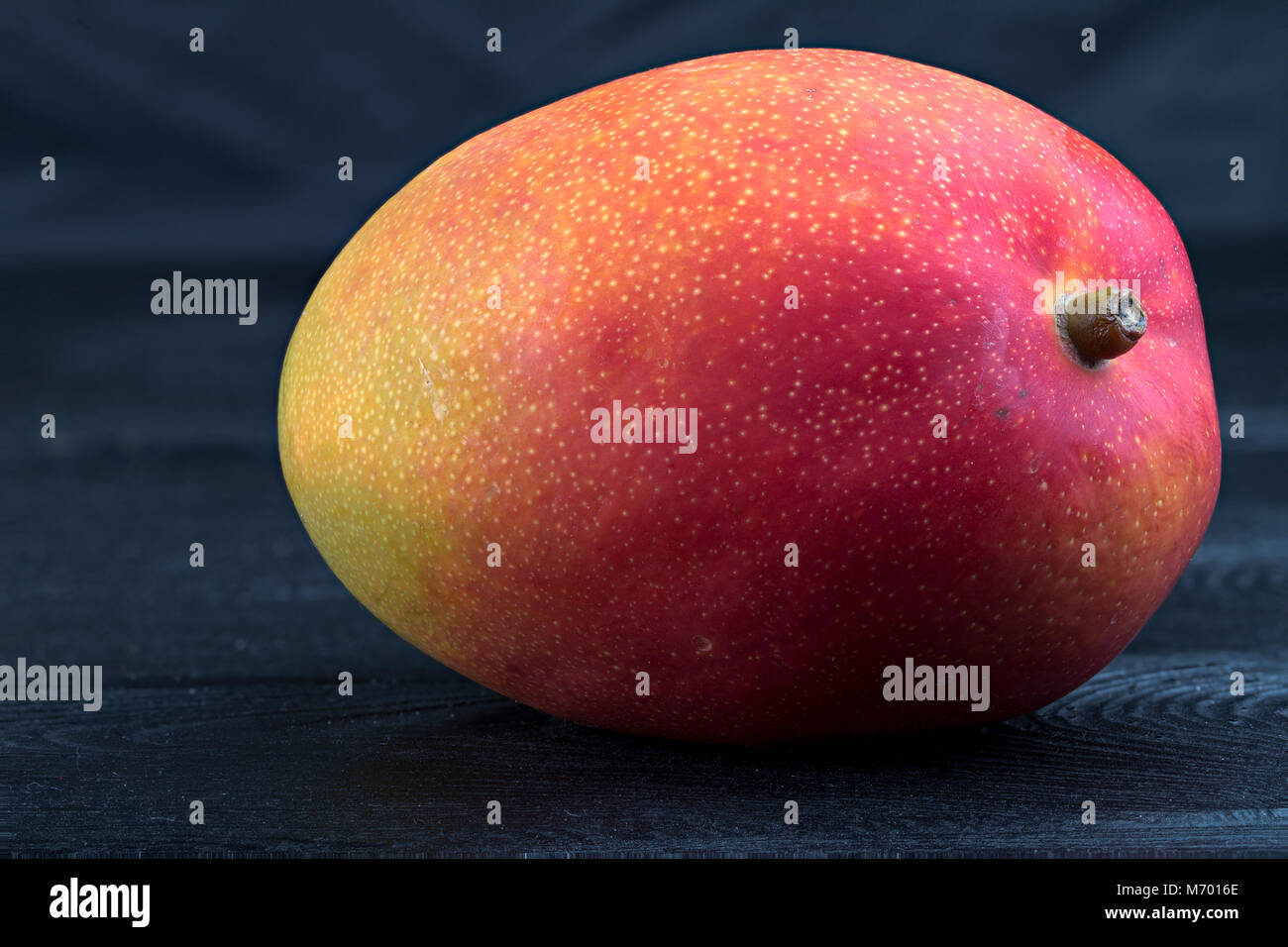 A mango fruit on a black wooden table Stock Photo - Alamy