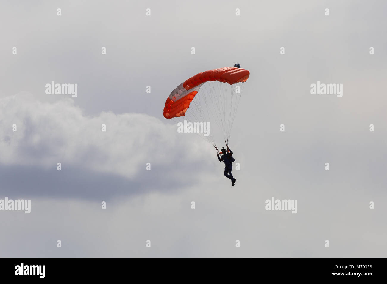 Parachutist with Orange Parachute against Blue Sky preparing for ...