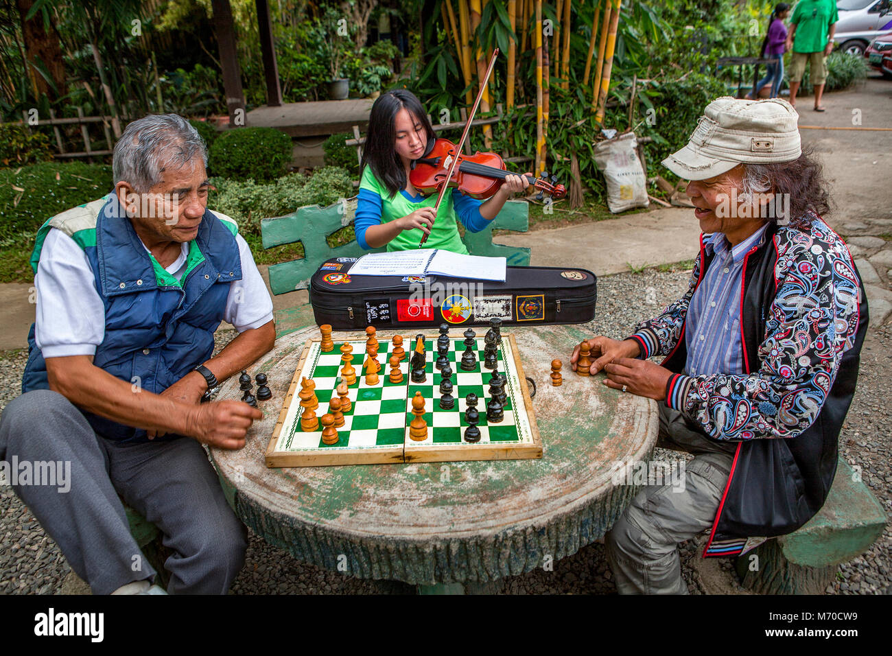 Two elderly Filipino men concentrate on their chess game while a young ...