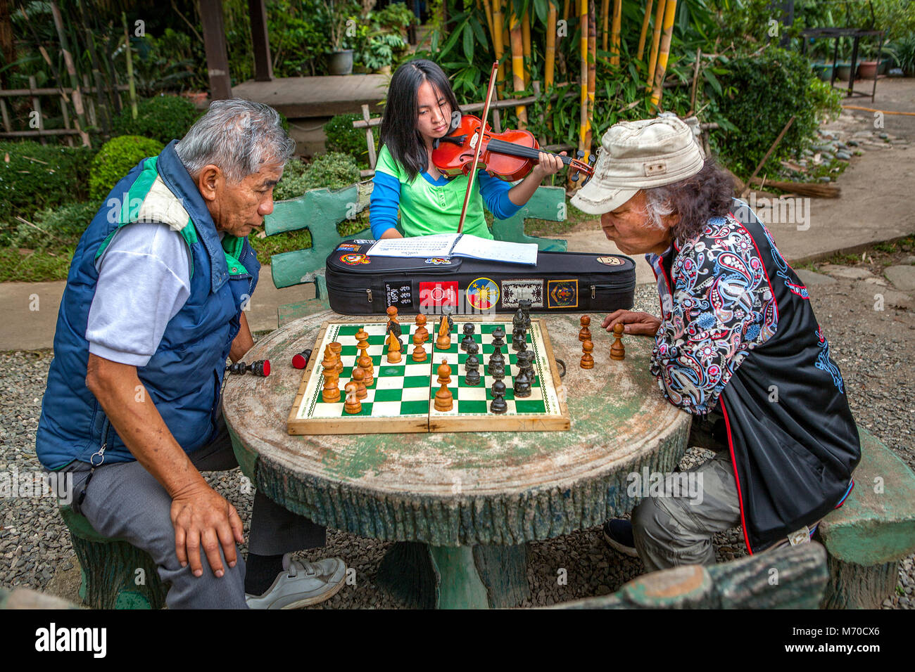 Two elderly Filipino men concentrate on their chess game while a young ...