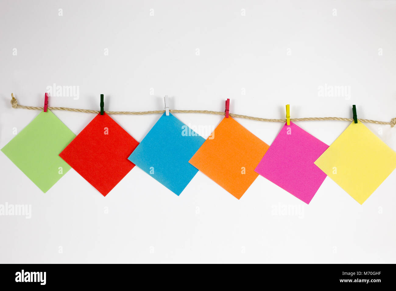Post-it notes with small colored pegs in a rope in white background ...