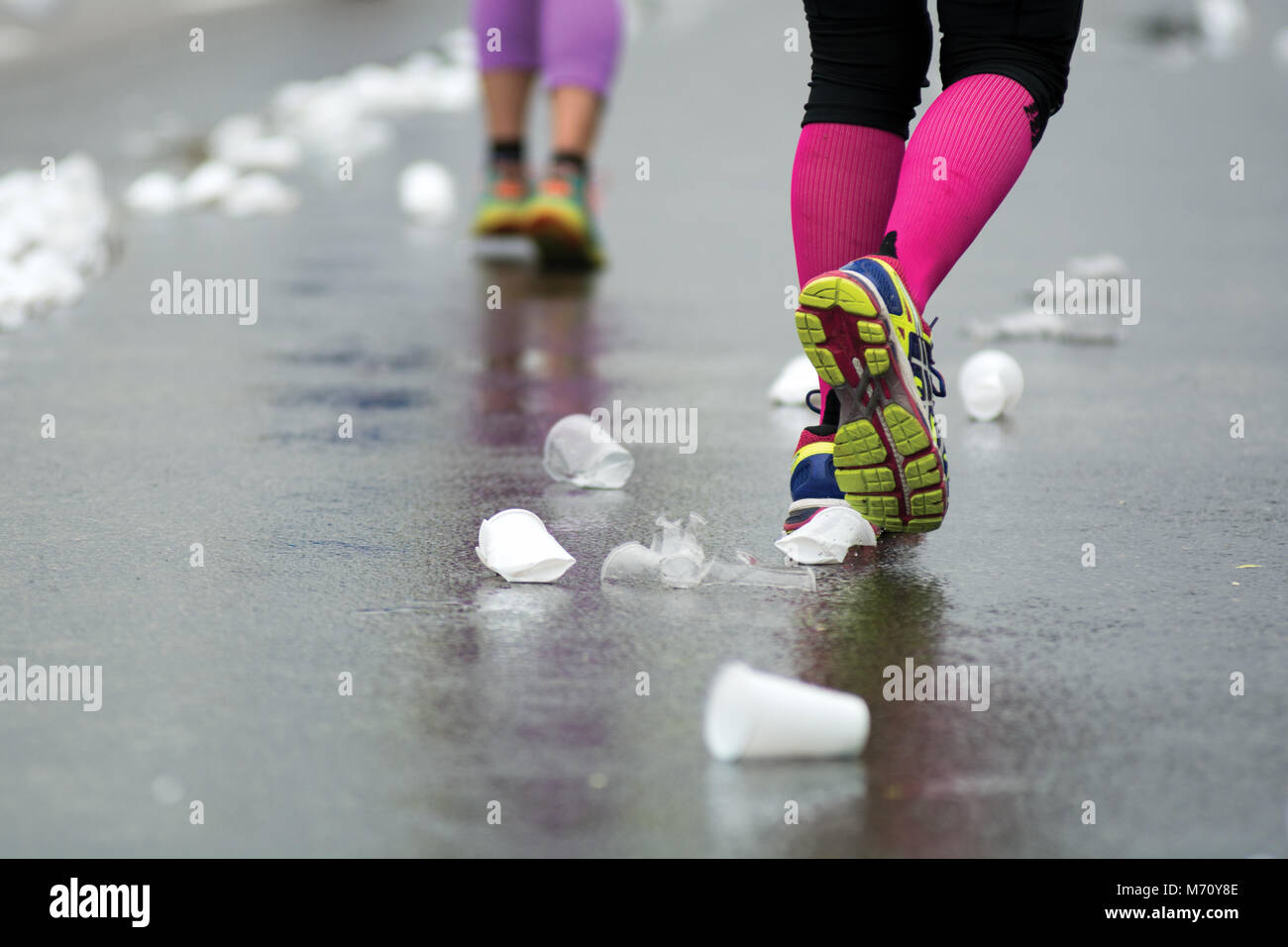 Runner's legs stepping on discarded plastic cups laying on the road ...