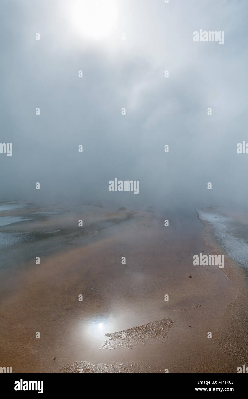 The sun reflects weakly through the mist rising from a geyser pool in ...