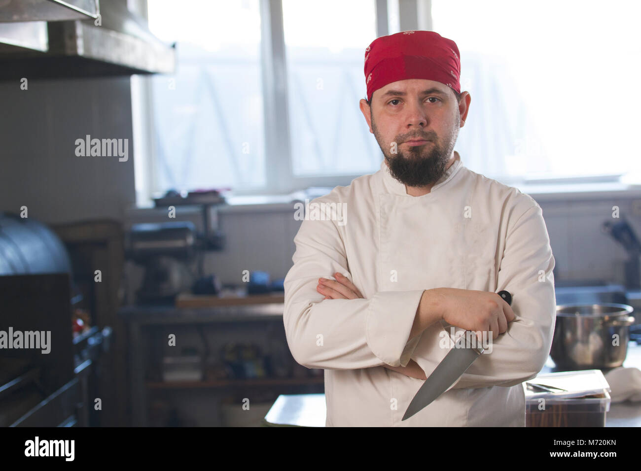 Portrait of a fashionable chef in bandana holding a knife in a kitchen ...