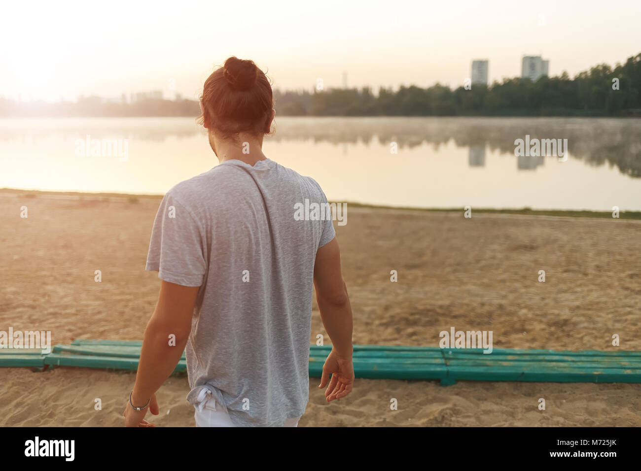 Young man back view, on the lake while looking at the sunrise on the ...
