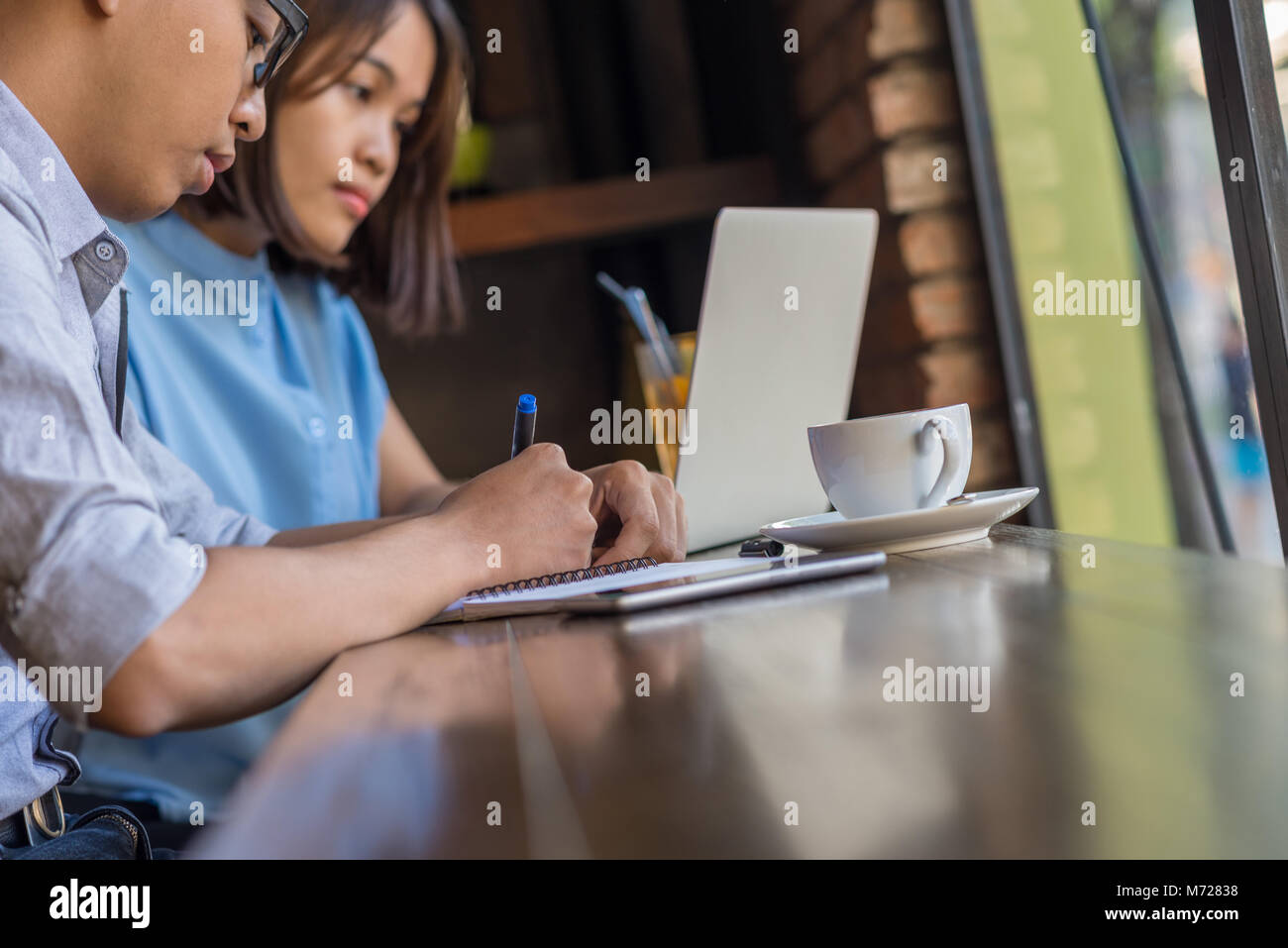 Two employees writing notes and working on laptop Stock Photo - Alamy