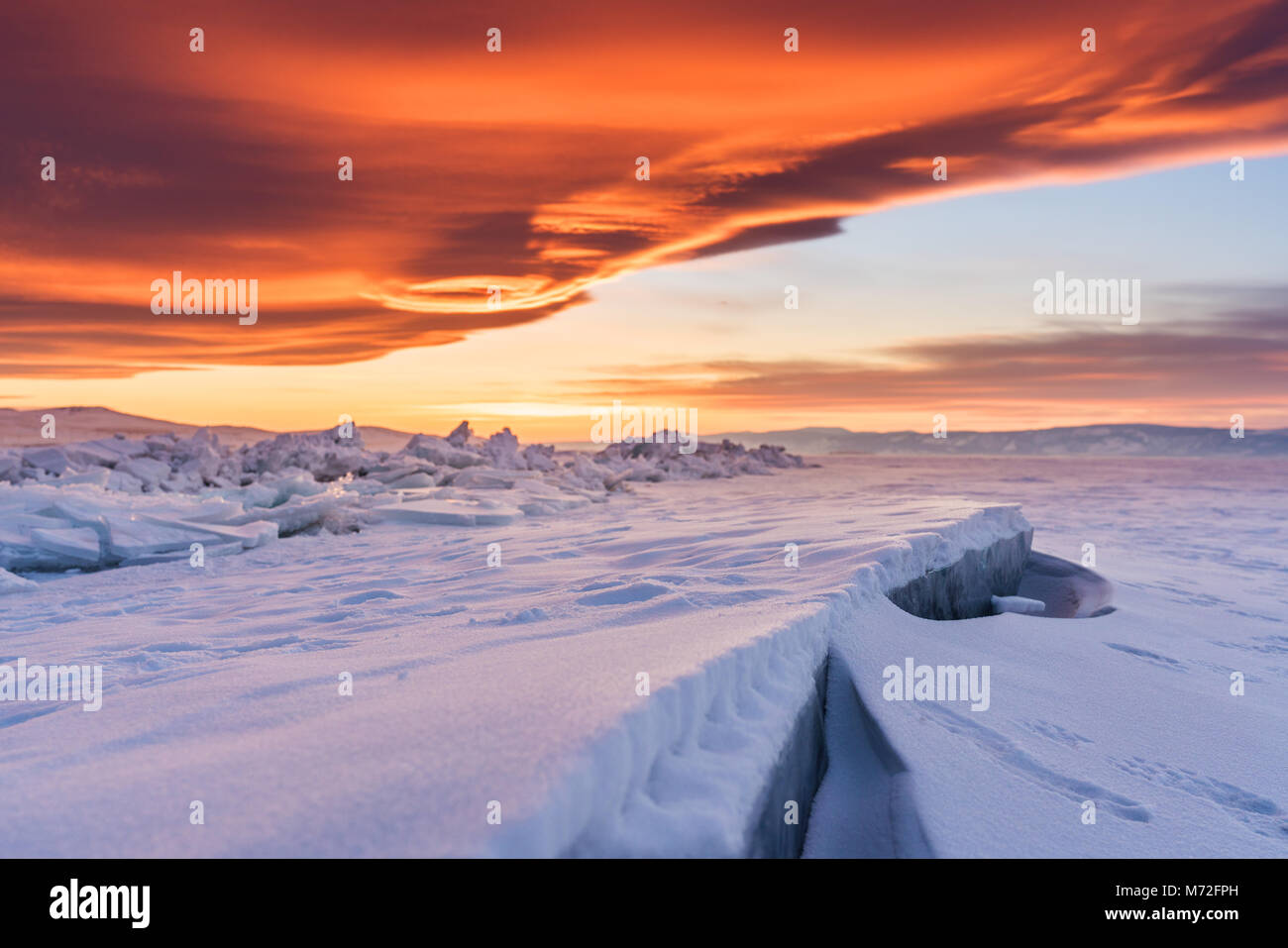 Winter landscape, cracked frozen lake ground covered of snow in sunset ...