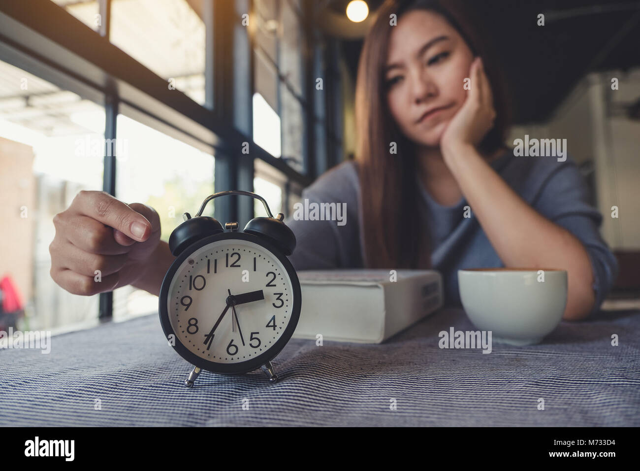 An asian woman pointing at a black clock with feeling bored while ...
