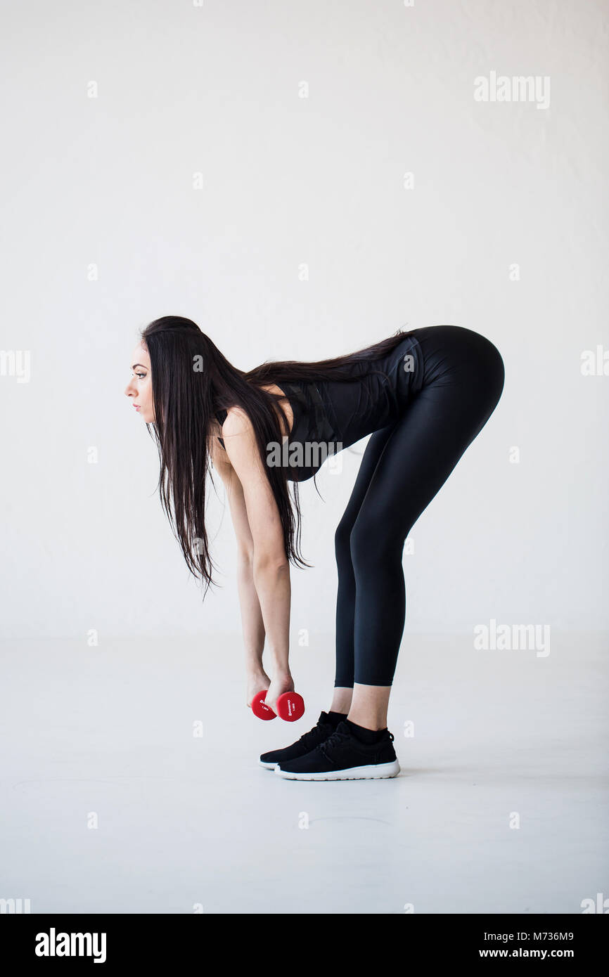 Slim muscular brunette is bending with the red dumbbells in the studio ...