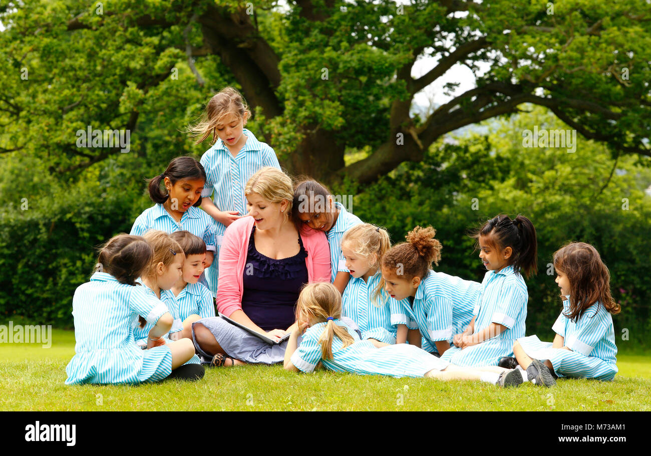 Primary schoolchildren gathered around their teacher outside under an ...