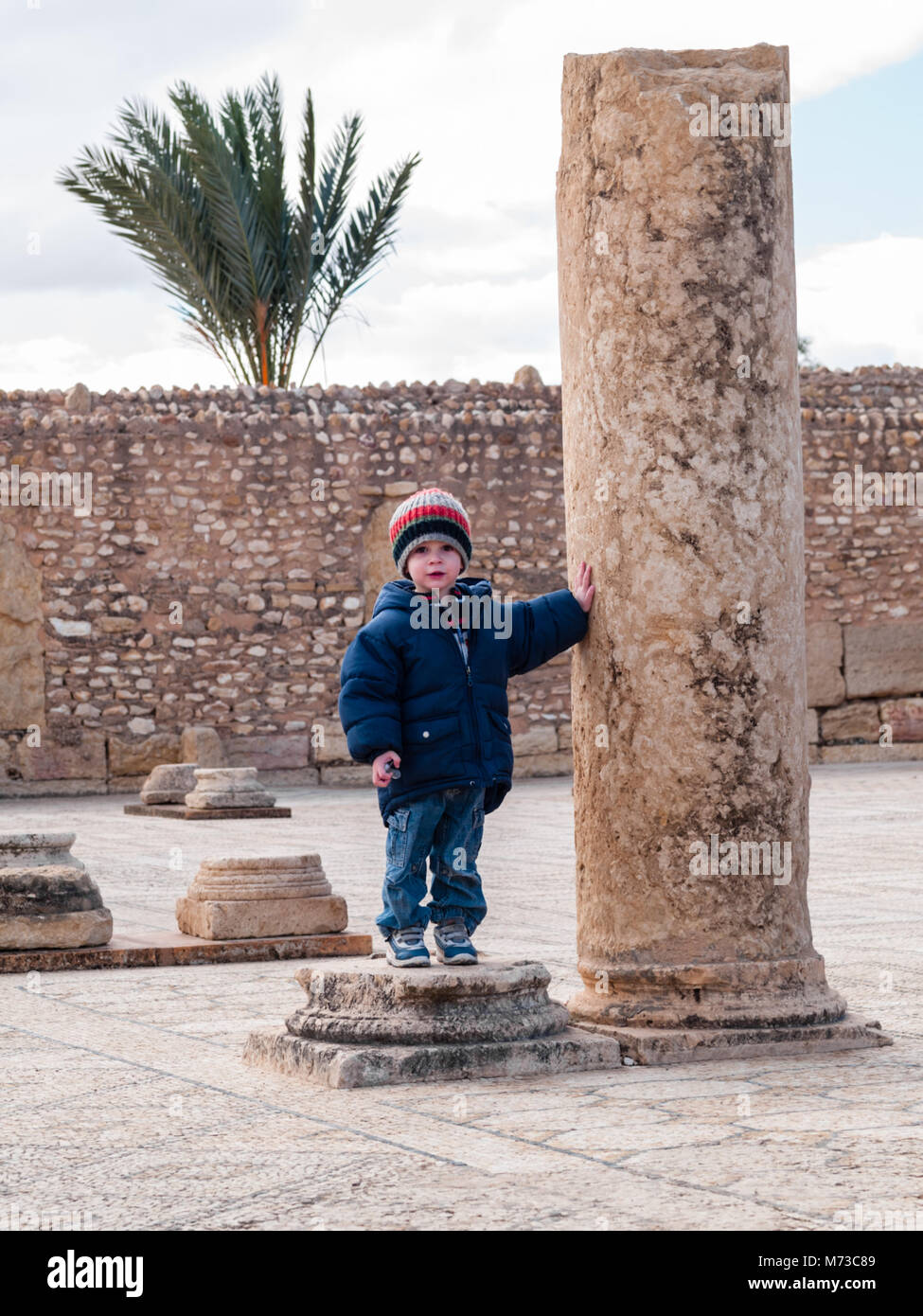 child leaning on an ancient column in ancient Roman archaeological site ...