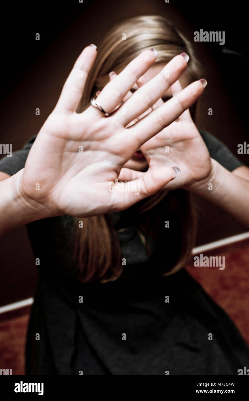 young woman with hands in front of her face, protecting herself from ...