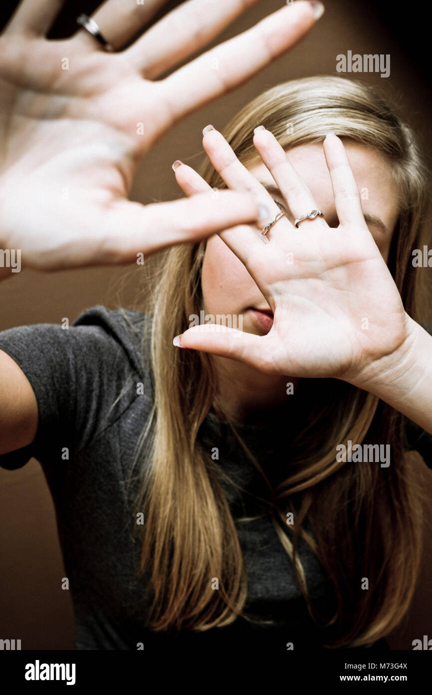 young woman with hands in front of her face, protecting herself from ...