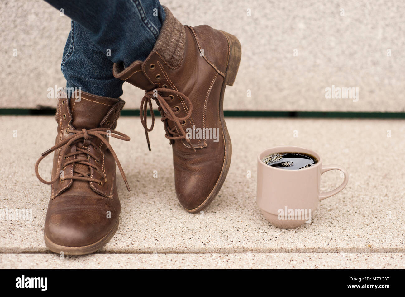 a mug of coffee on the ground, near the legs of a girl in jeans and ...