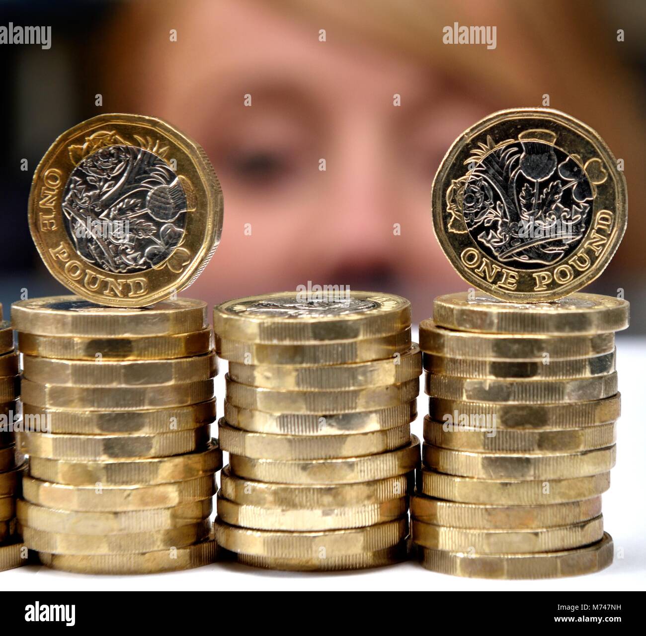 Stacks of one pound coins close up with woman's face in the background ...