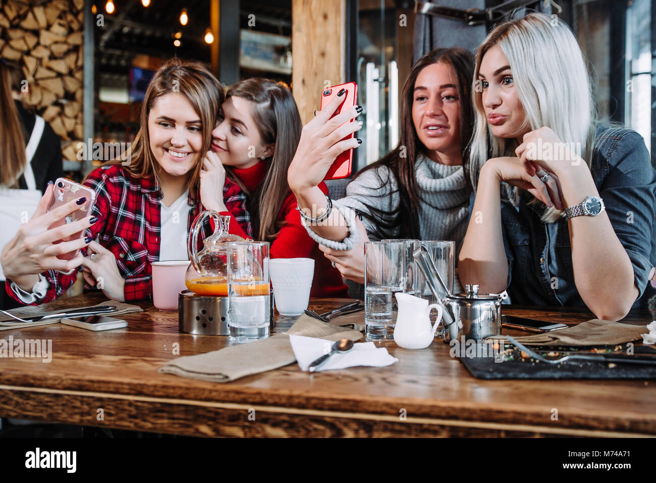Four friends sitting by the table in cafe and making selfie on ...