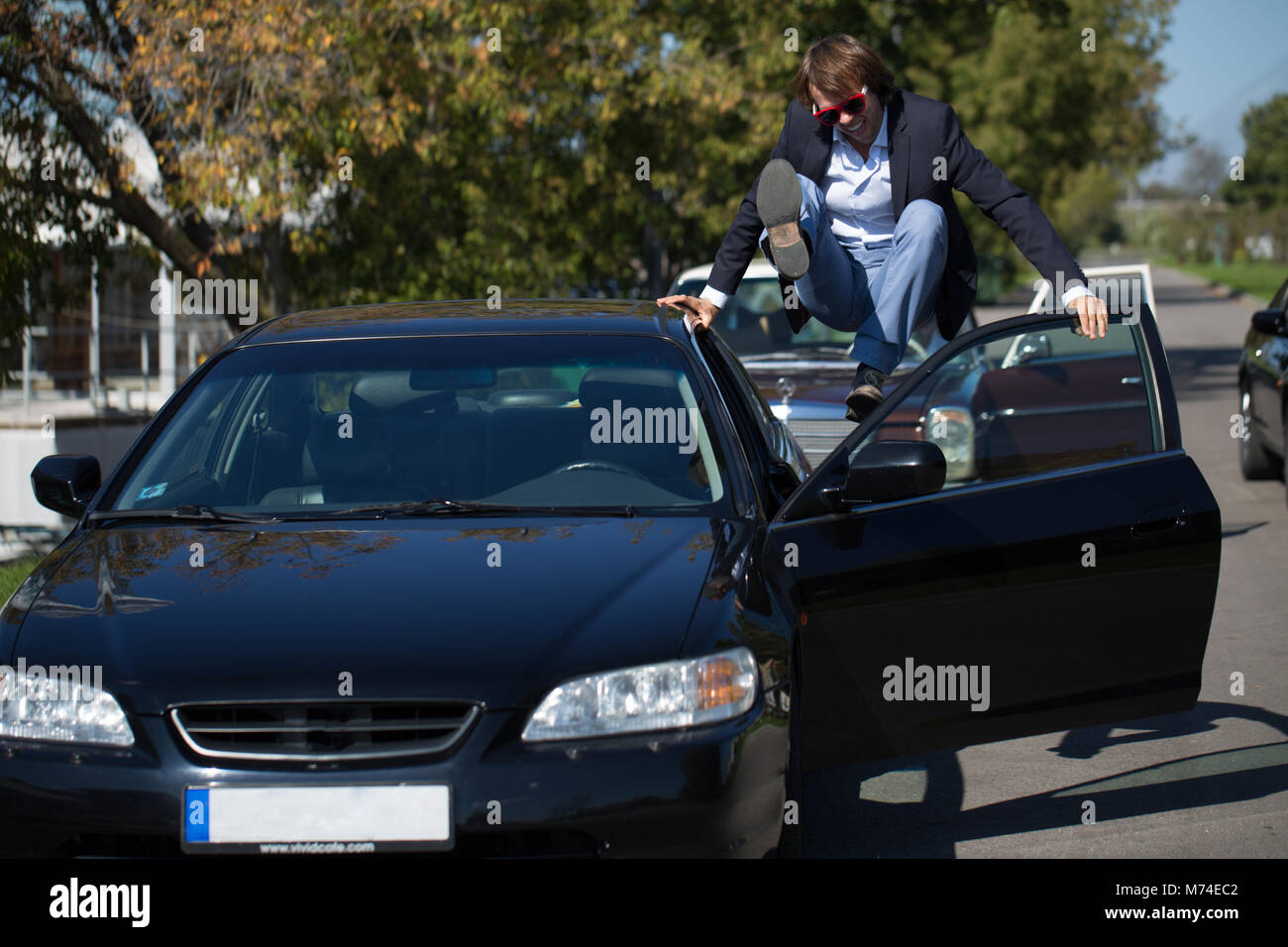 Man near black car in suit jumping Stock Photo - Alamy