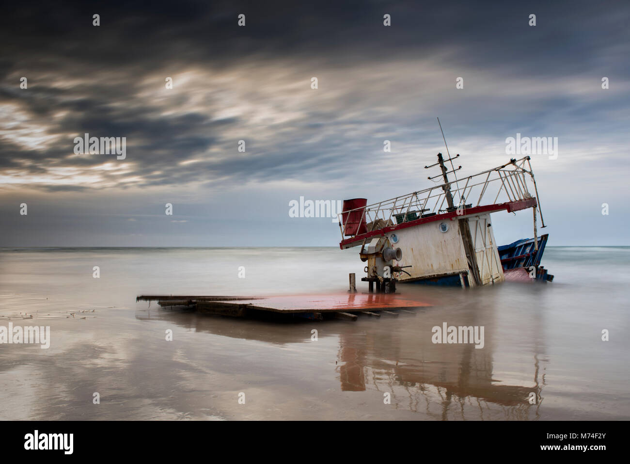 The broken ship along with the sea on a sandy beach and sunset twilight ...