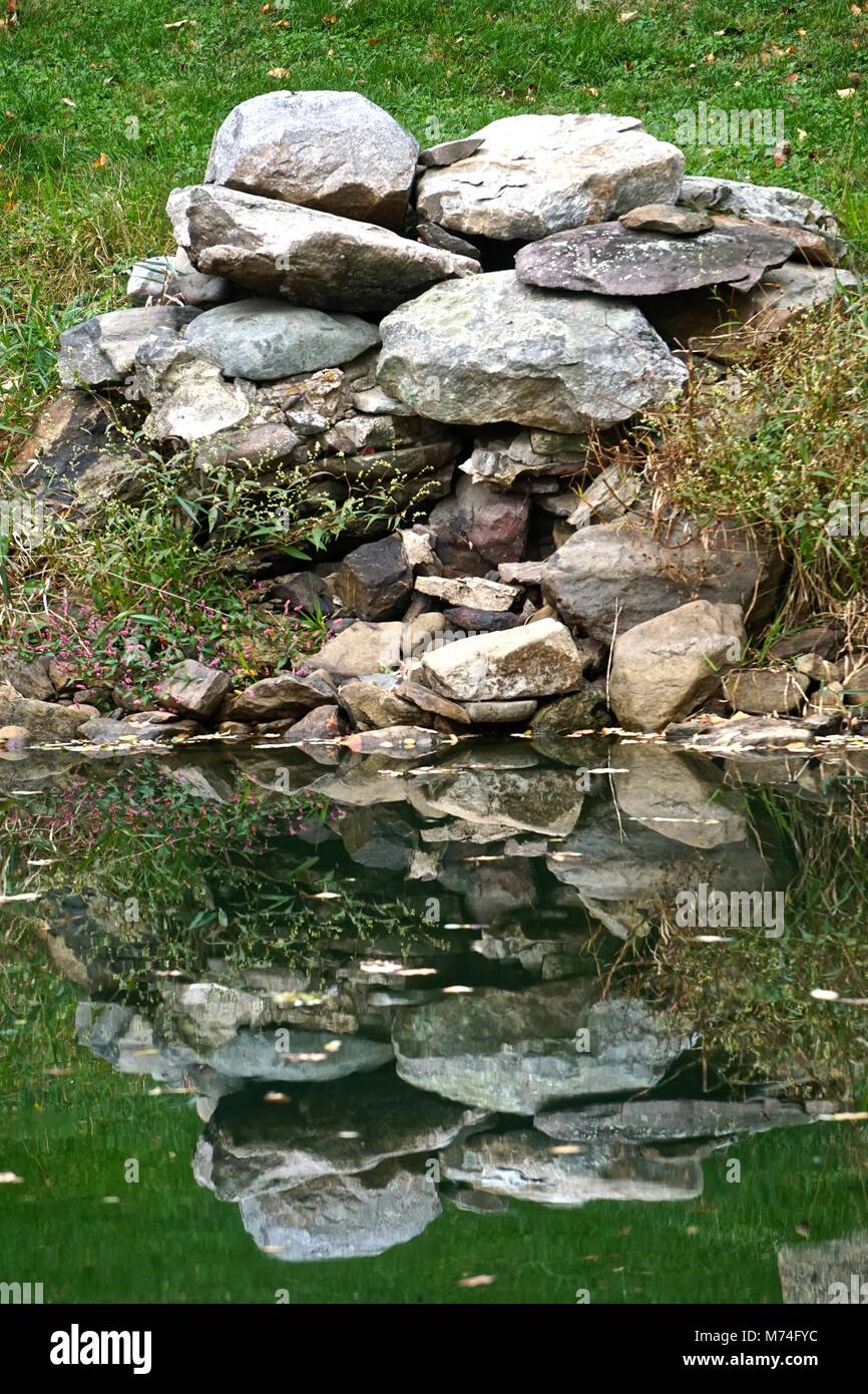 A pile of rocks on a grassy bank reflected in a stream Stock Photo - Alamy
