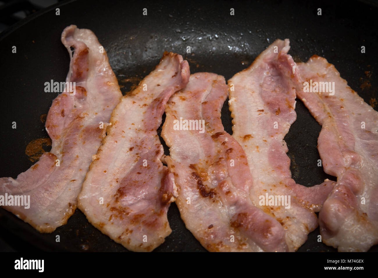 Streaky bacon cooking in the frying pan Stock Photo - Alamy