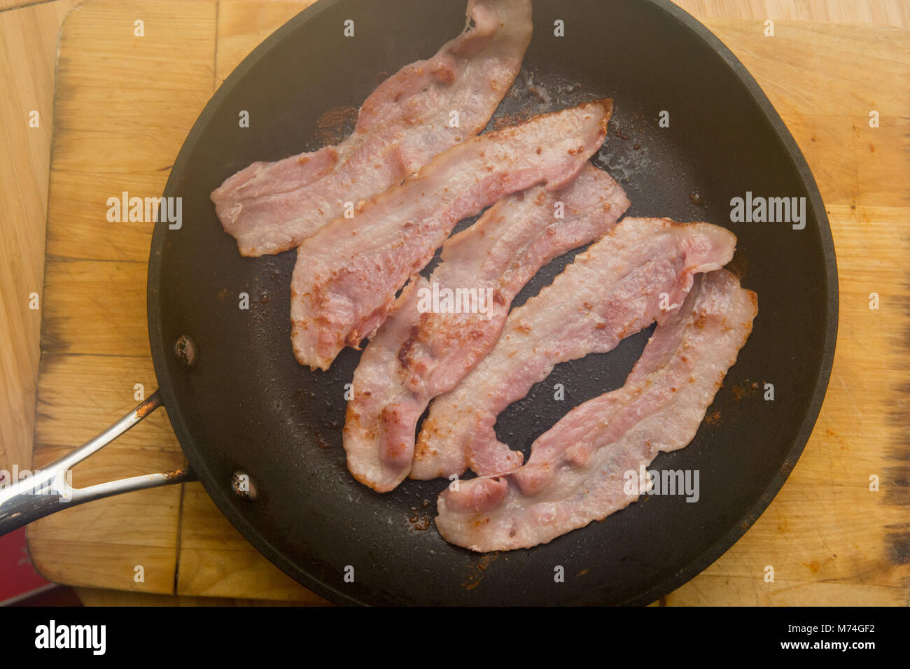 Streaky bacon cooking in the frying pan Stock Photo - Alamy