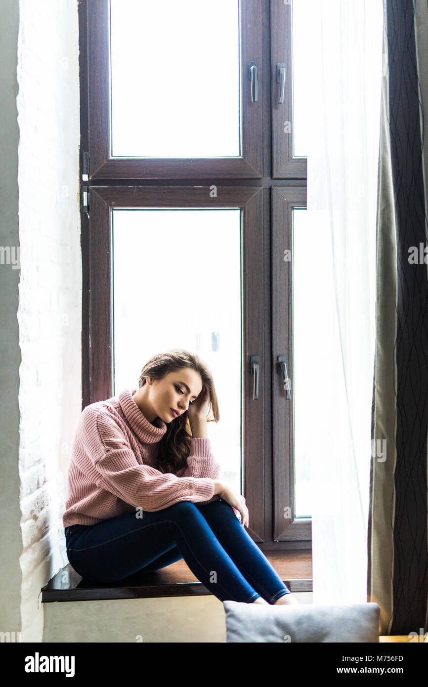 Beautiful young woman looking through window while sitting at ...