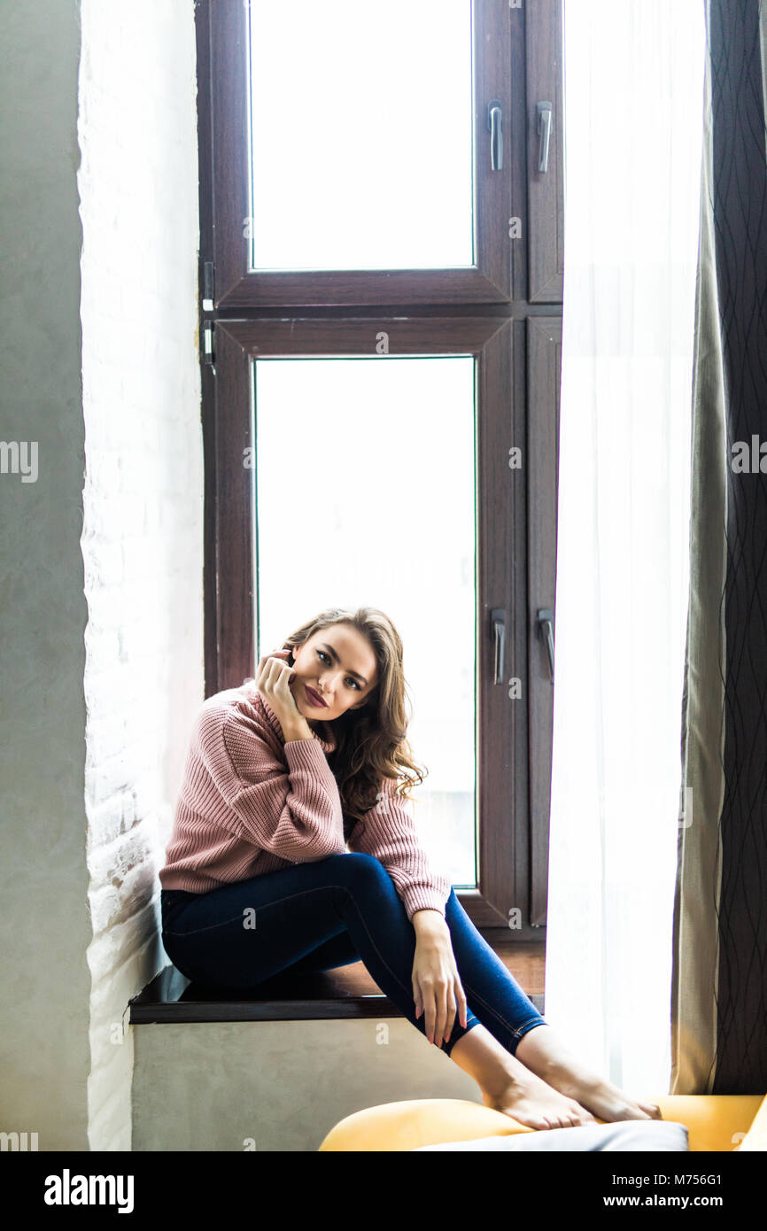 Beautiful woman looking through window while sitting at windowsill at ...