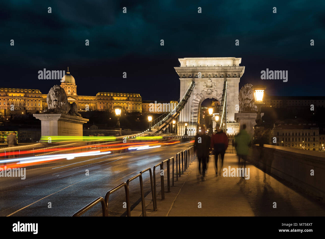 Chain bridge at night with traffic lights and walking blurred people ...