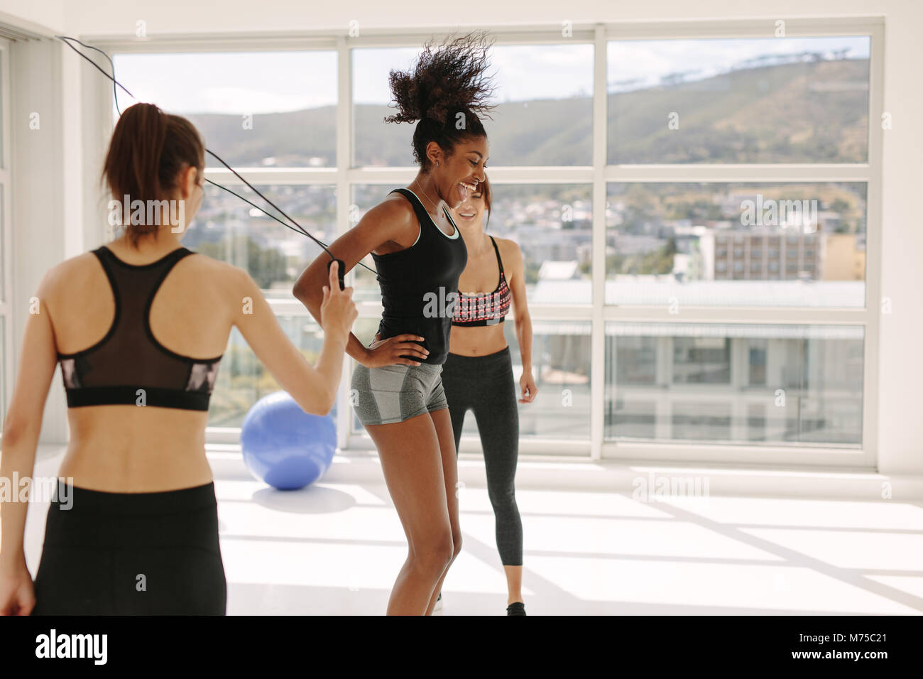 Smiling woman jumping rope with friends in fitness studio. Female doing ...