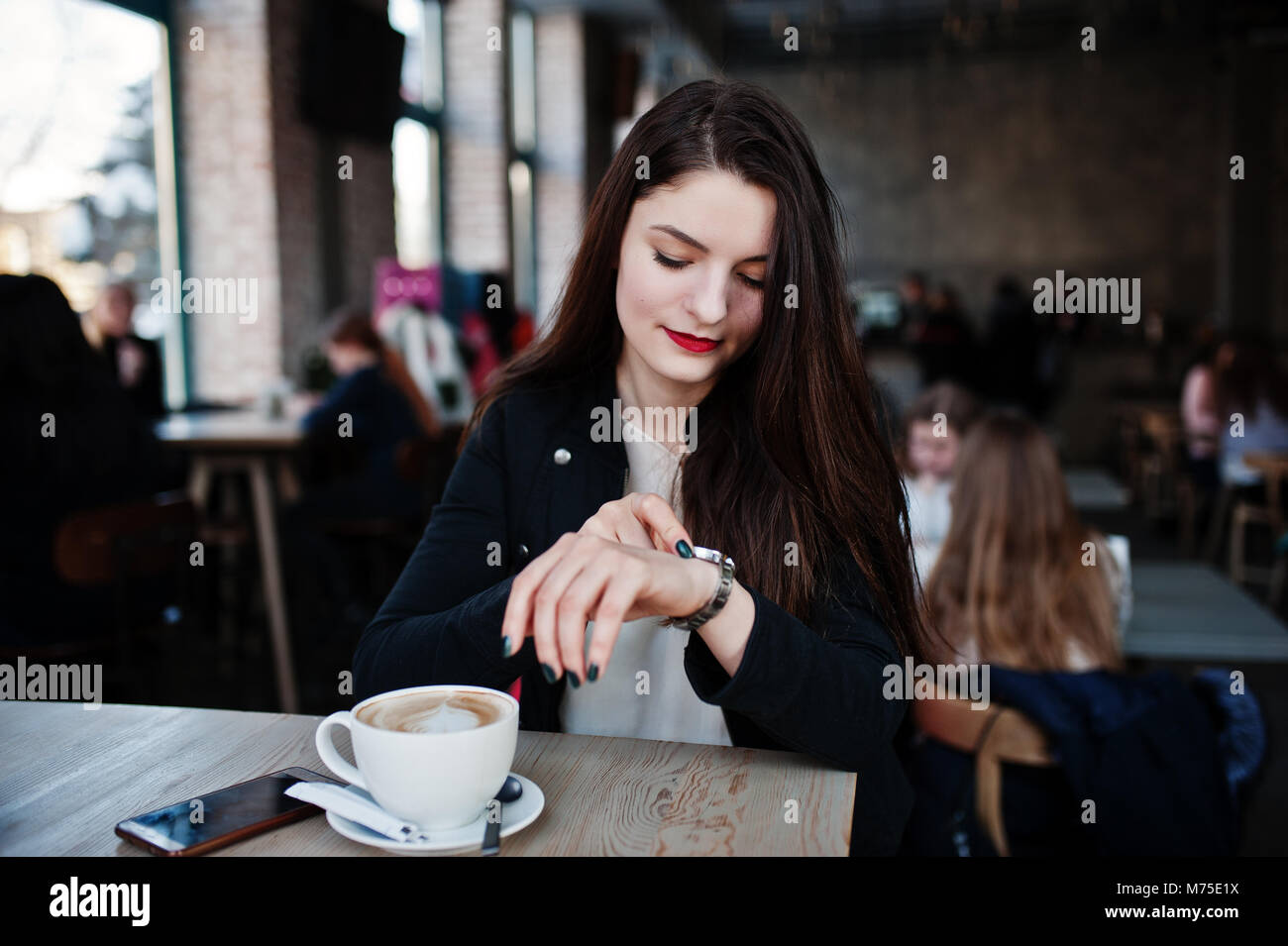 Brunette girl sitting on cafe with cup of cappuccino and looking at her ...