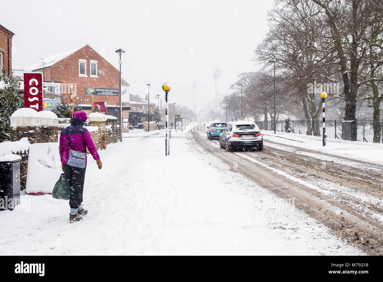 Winter snowfall. Person walking alone through a town centre in falling ...