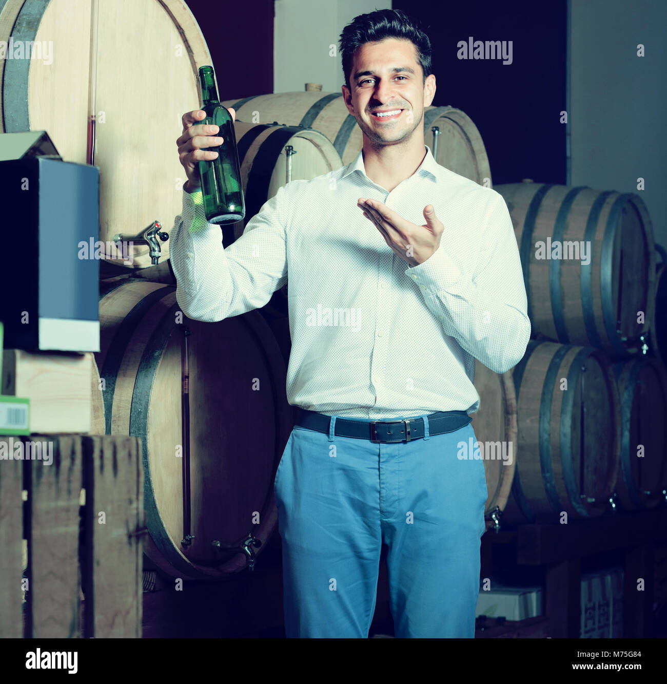 smiling man choosing bottle of white wine in shop with woods Stock ...