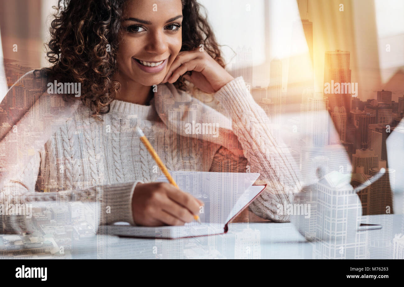Cute young woman smiling while writing important information in her ...