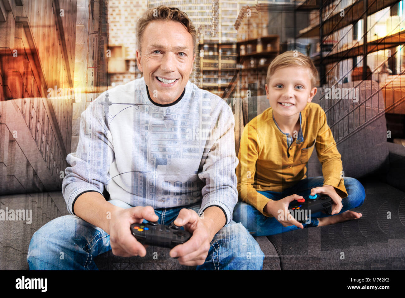 Happy father smiling while playing video games with his cheerful son ...