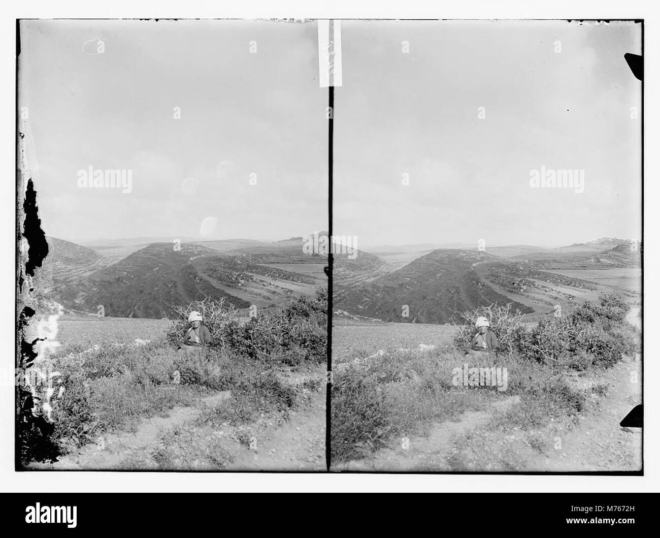 A photograph of a man seated in a hilly landscape, capturing a moment ...