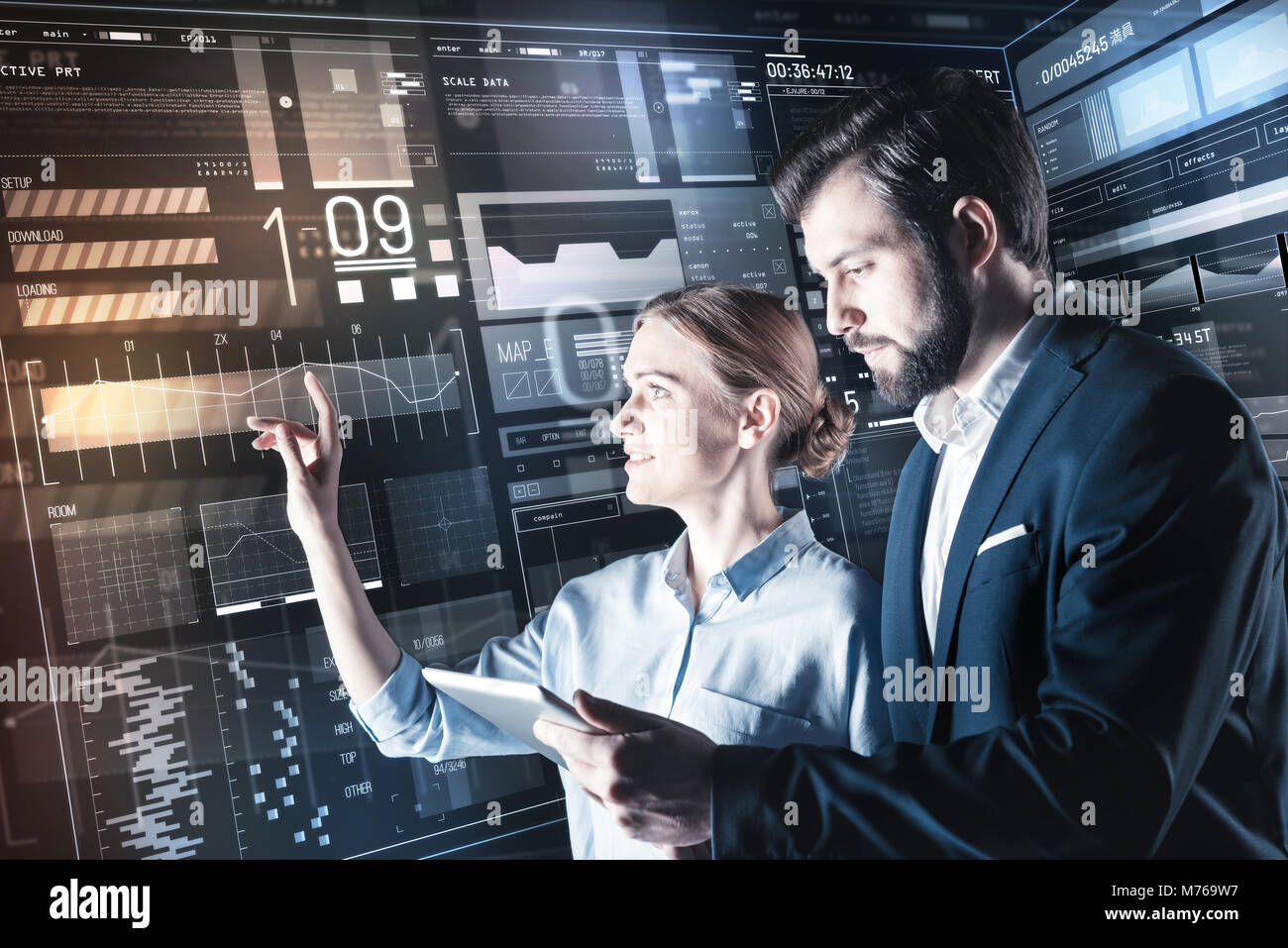 Cheerful woman pointing to the screen while her calm colleague being ...