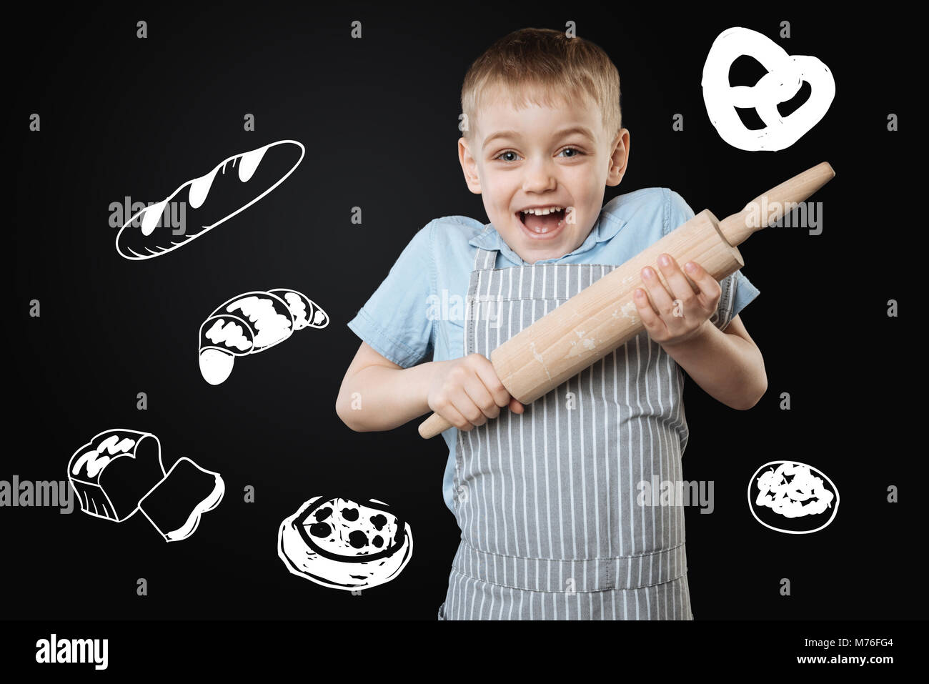 Emotional boy holding a rolling pin and feeling excited while cooking ...
