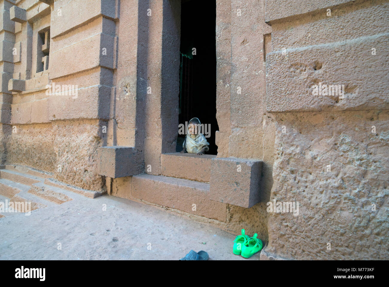 A young girl wearing a white robe looking through the doorway of a rock ...