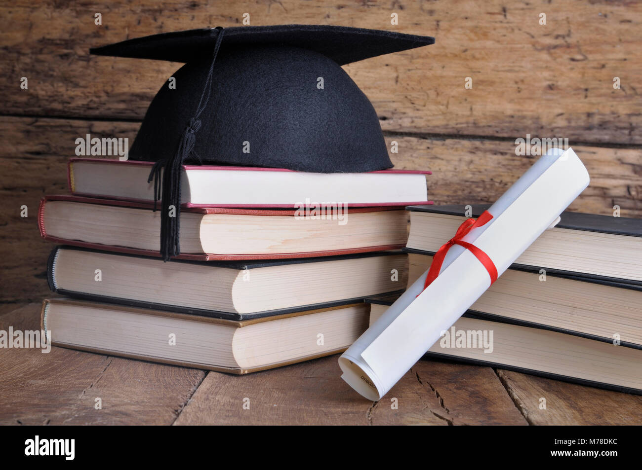 Graduate rolled up in a red ribbon and a black hat on pile of book on ...