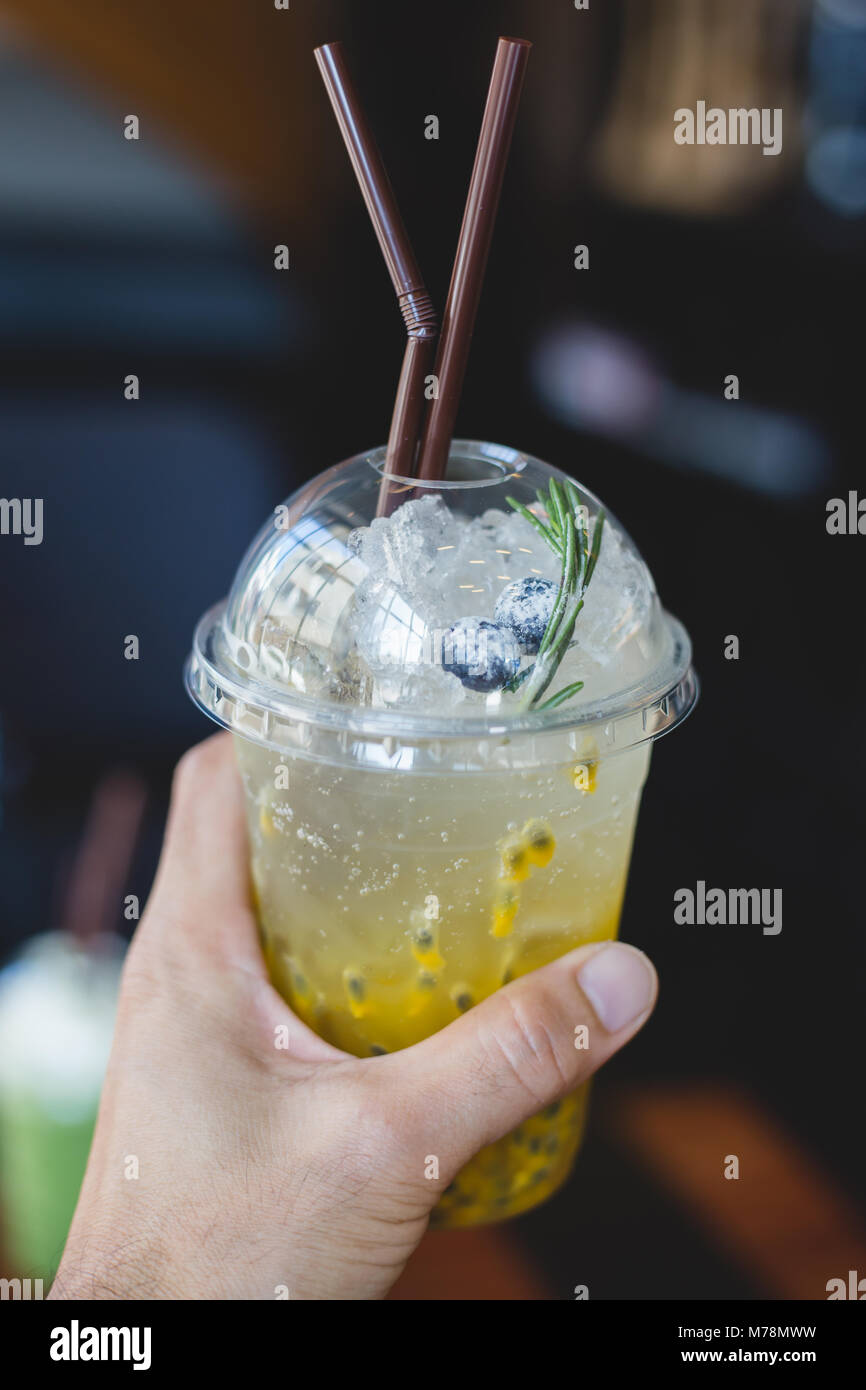 Hand holding passion fruit with soda on plastic glass with two straw in ...