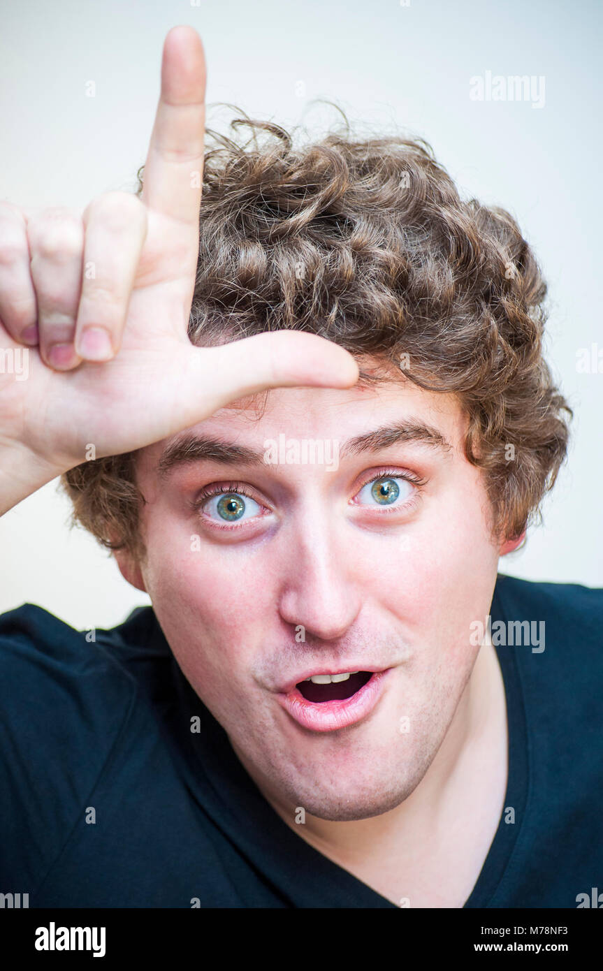 Portrait of young funny curly man showing loser hand sign on camera on ...