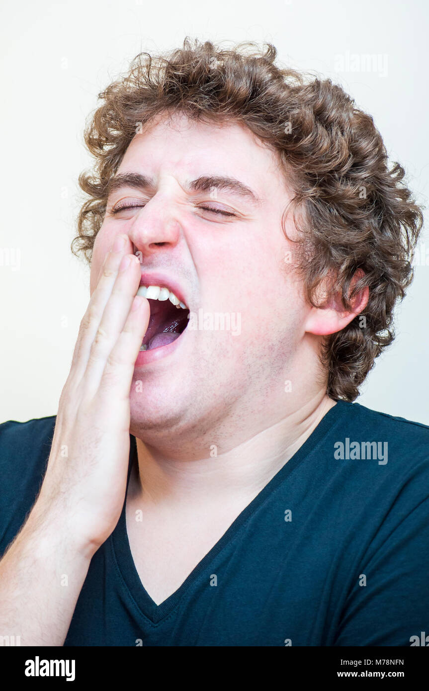 Portrait of young Caucasian Ethnicity tired yawning curly man covers ...