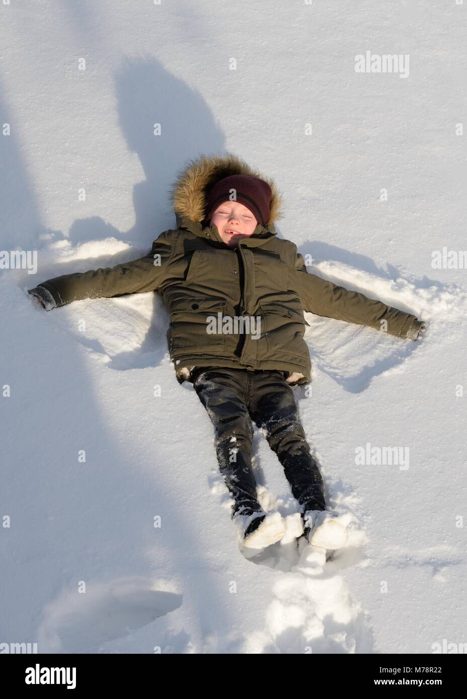 A young boy lying on his back in deep snow making angel wings shot from ...