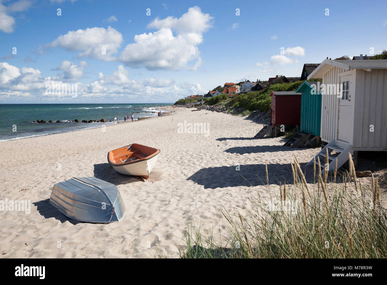 Boats and beach huts on white sand beach with town behind, Tisvilde ...