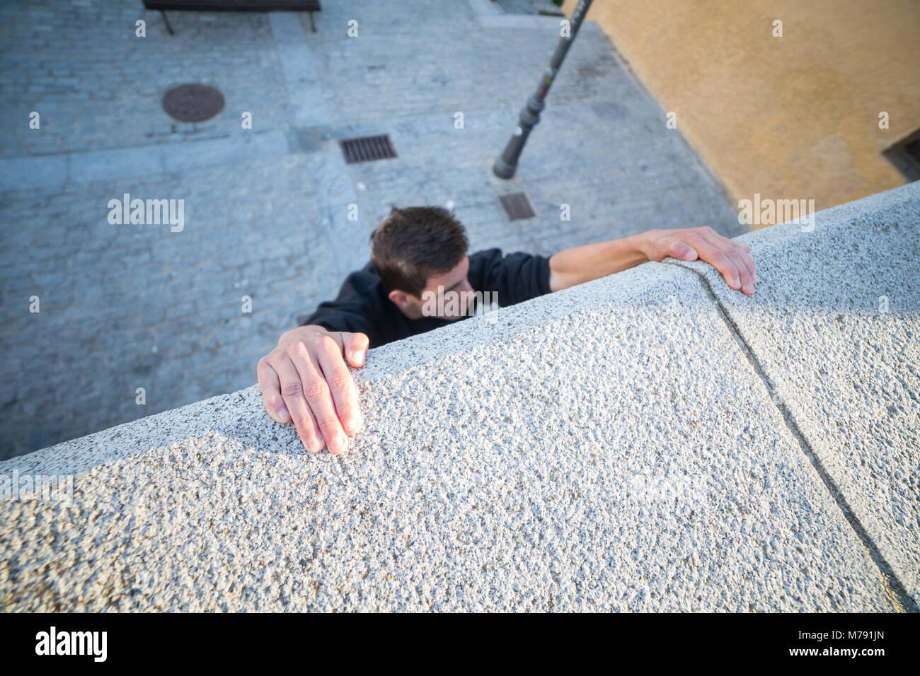 Young man hanging on wall on hands and trying to climb up while doing ...