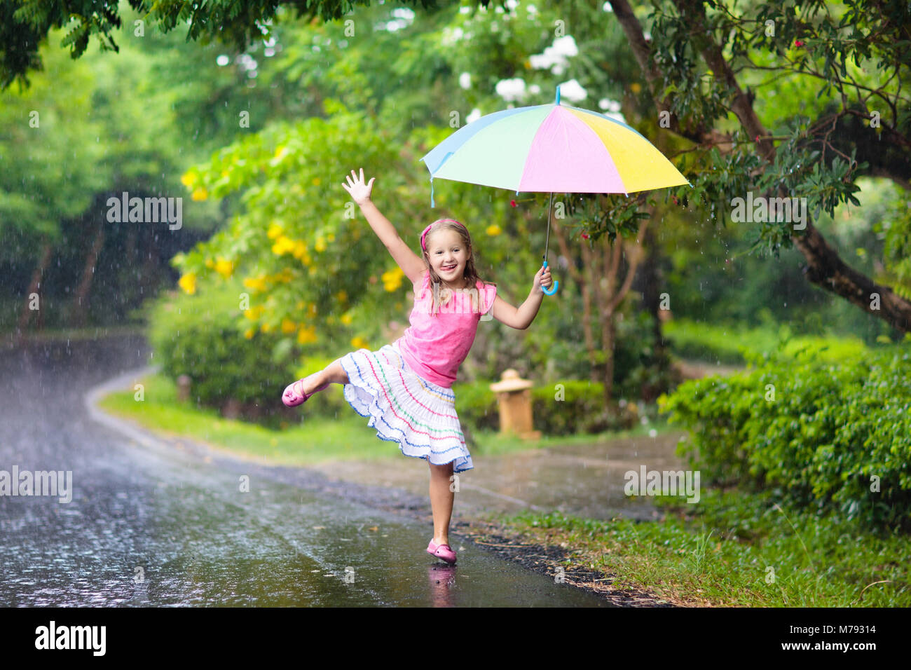 Kid playing out in the rain. Children with umbrella play outdoors in ...