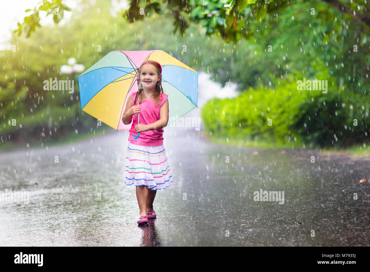 Kid playing out in the rain. Children with umbrella play outdoors in ...