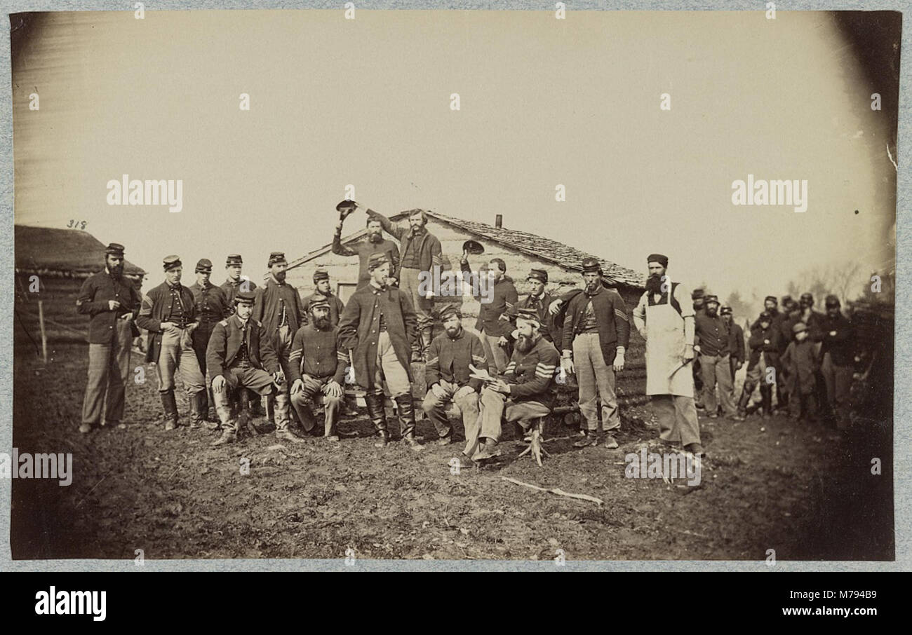 The photograph shows a group of soldiers gathered outside a cabin ...
